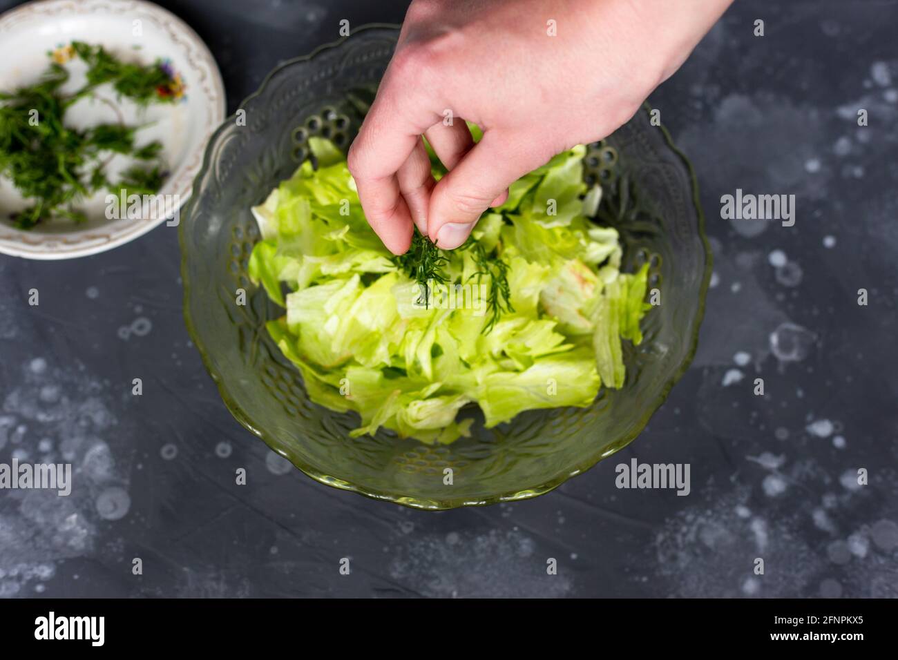 Adding greens to salad in a glass plate on a gray table Stock Photo - Alamy