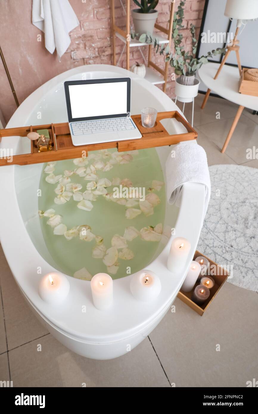 Stylish interior of modern bathroom with laptop and burning candles ...