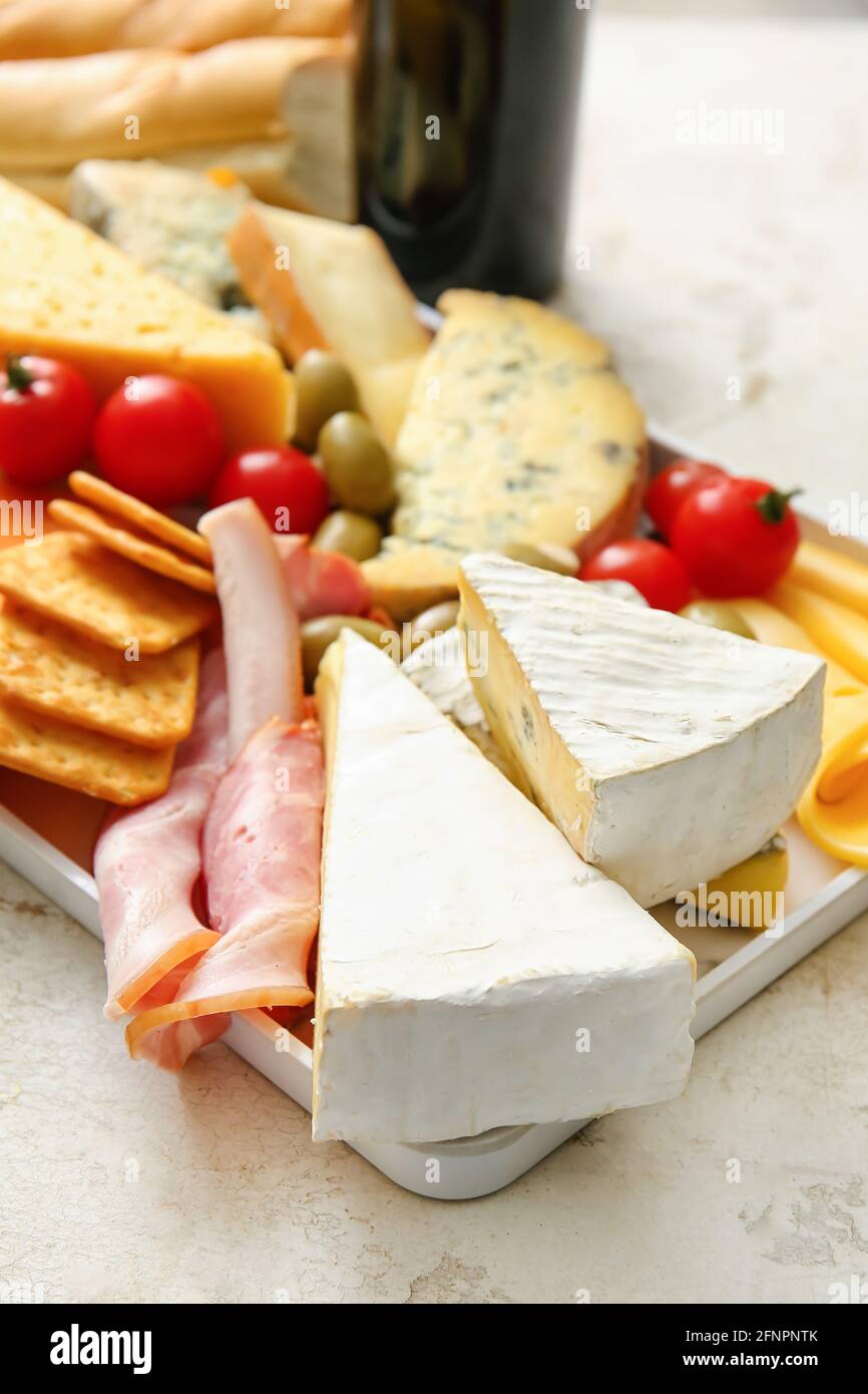 Tray with different types of cheese and snacks on light background ...