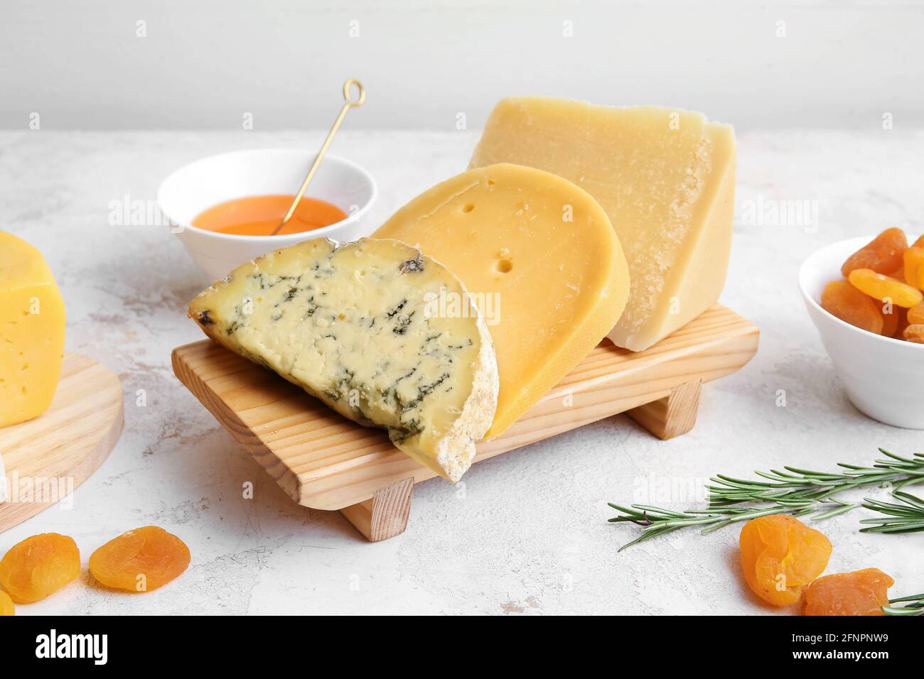 Different types of cheese, dried apricots and honey on light background ...
