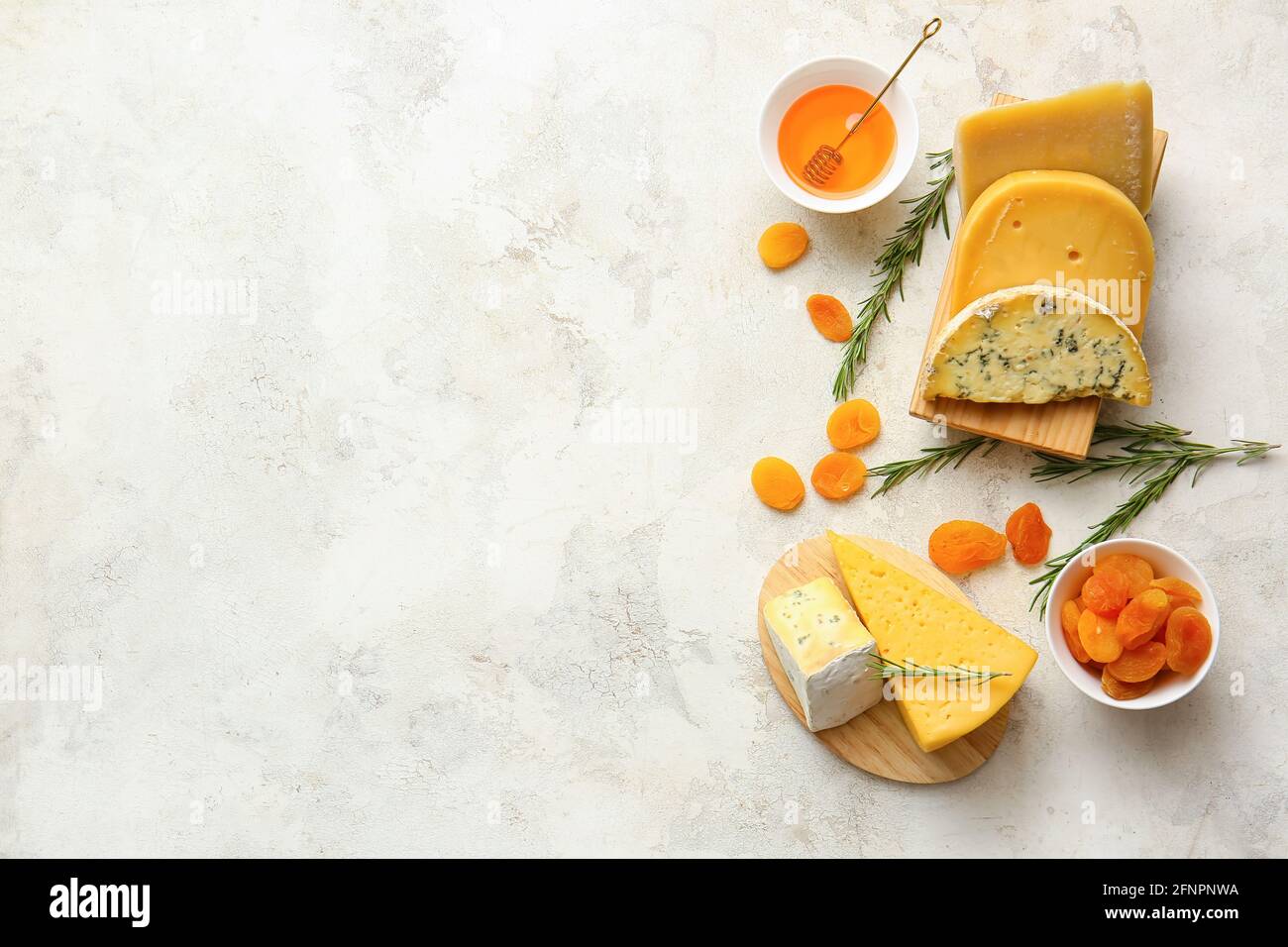 Different types of cheese, dried apricots and honey on light background ...