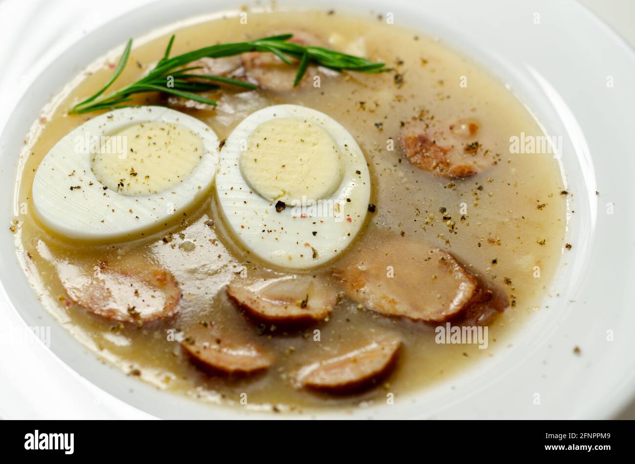 Traditional polish sour soup with sausage and eggs in a white deep ...