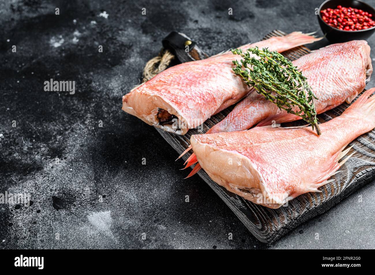 Whole raw red snapper fish on a cutting board. Black background. Top ...