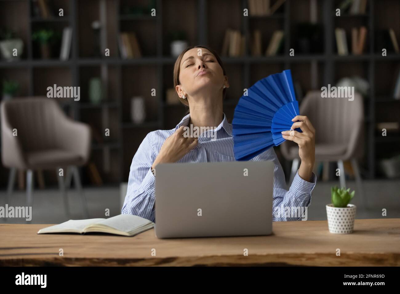 Young woman sit by laptop at hot office use fan Stock Photo - Alamy
