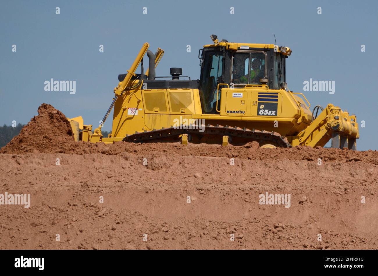 A worker uses a Komatsu 65EX crawler bulldozer to move dirt at a ...