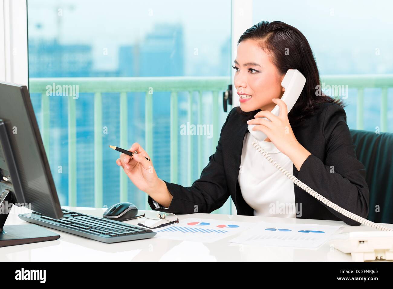 Asian Chinese business woman telephoning in office controlling profit ...