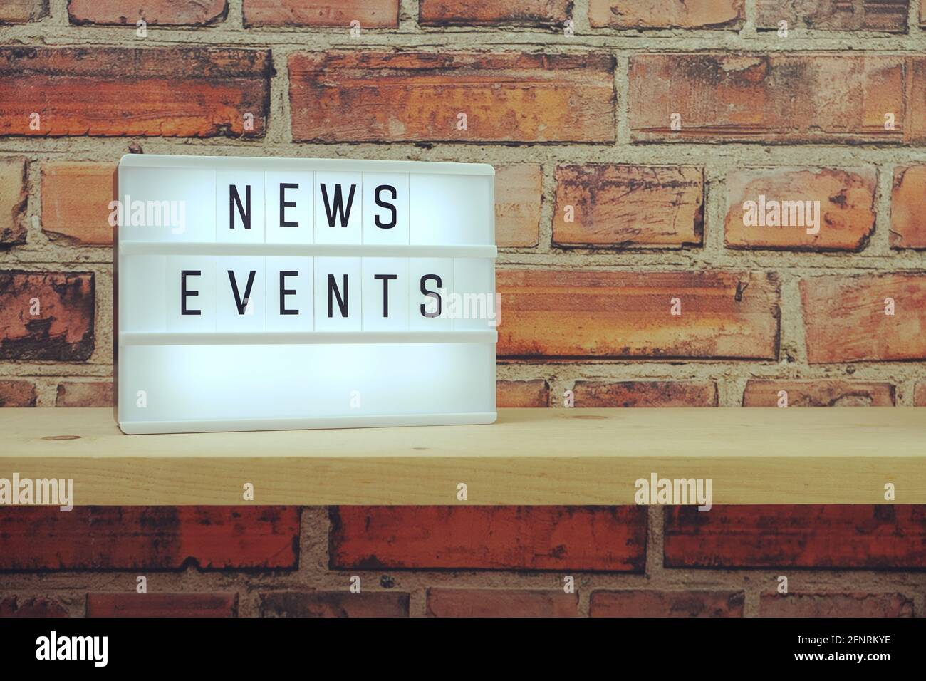 News Events word in light box on brick wall and wooden shelves ...