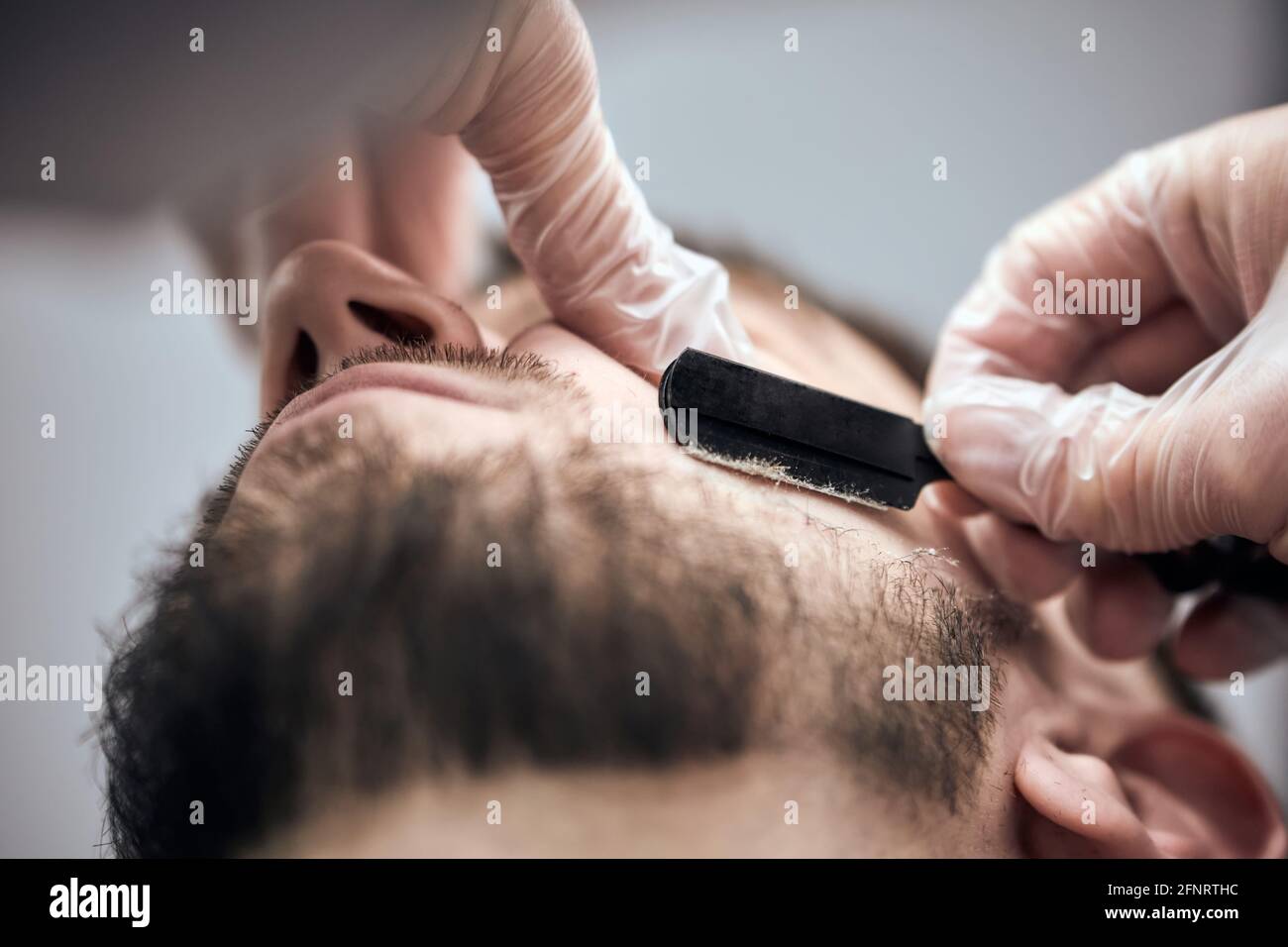 Professional barber shaves beard to young man using straight razor at ...