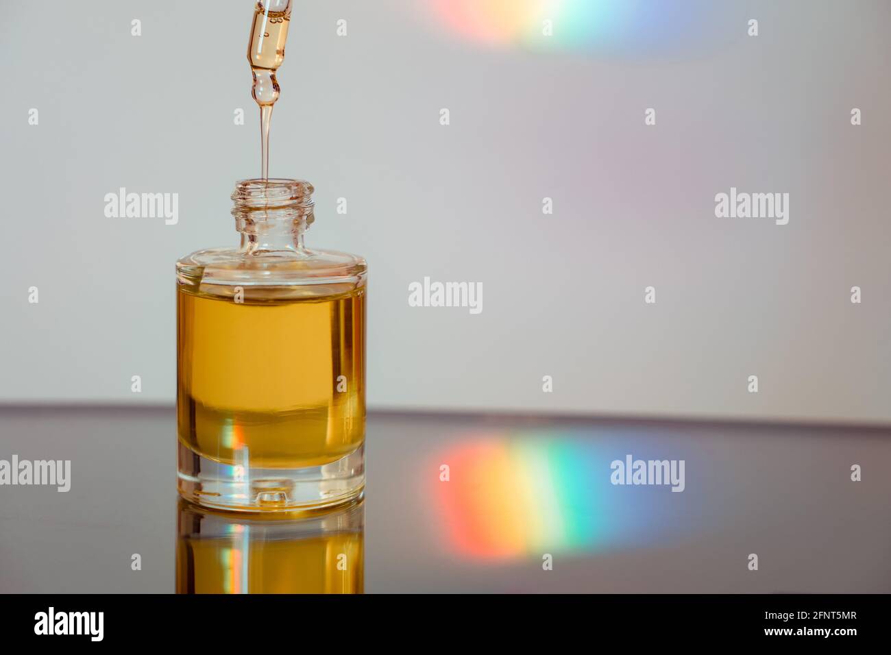 Face oil on reflective surface with a rainbow streak. Flowing serum ...