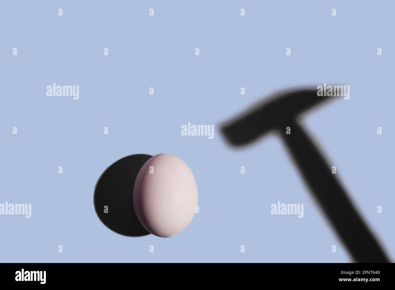 Minimal concept with an egg under the harsh light and a hammer shadow ...