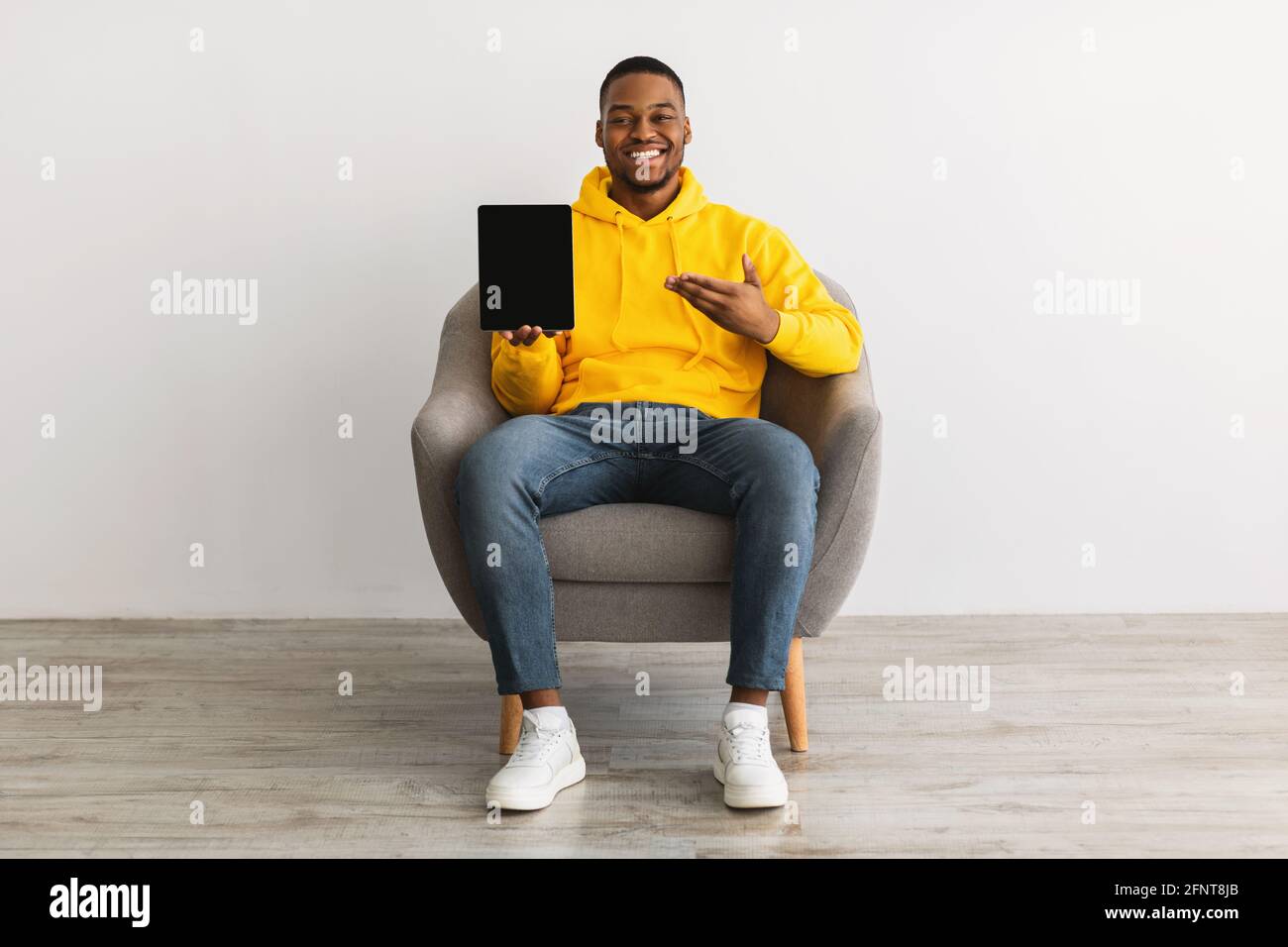 African Guy Showing Tablet Screen Sitting In Chair, Gray Background ...