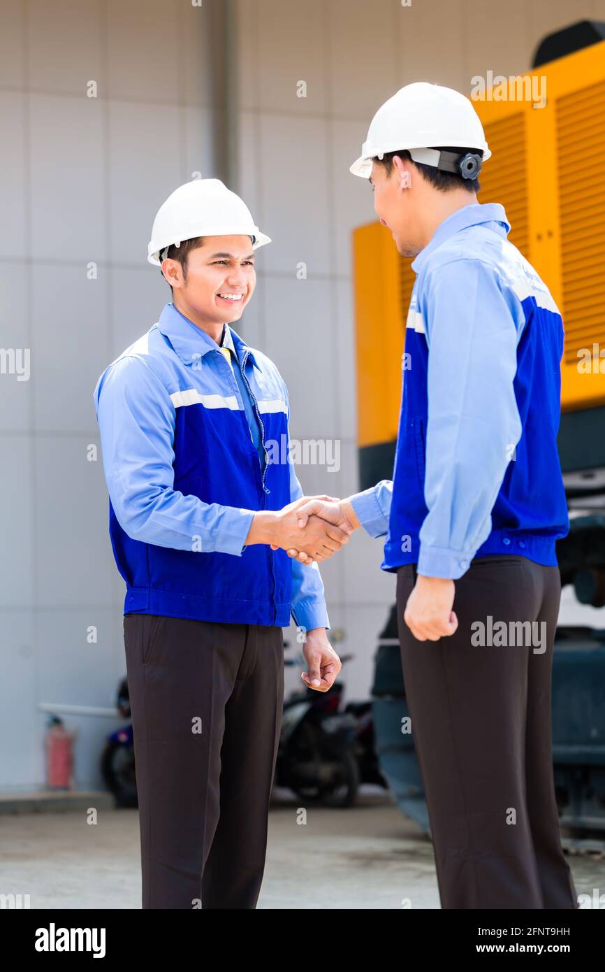 Asian engineer having agreement handshake at construction machinery of ...