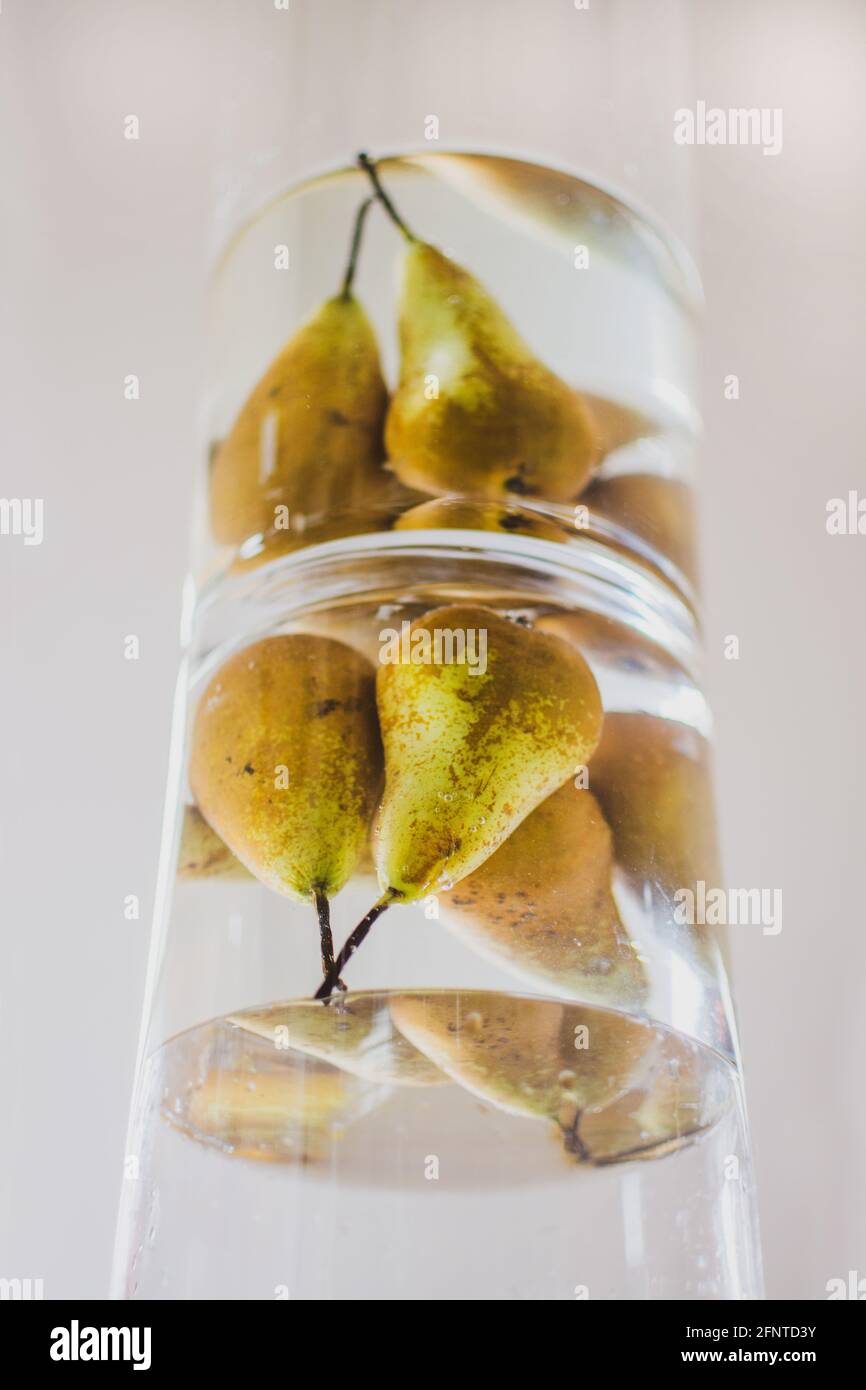 Yellow pears dipped in water inside a transparent jar reflected in a ...