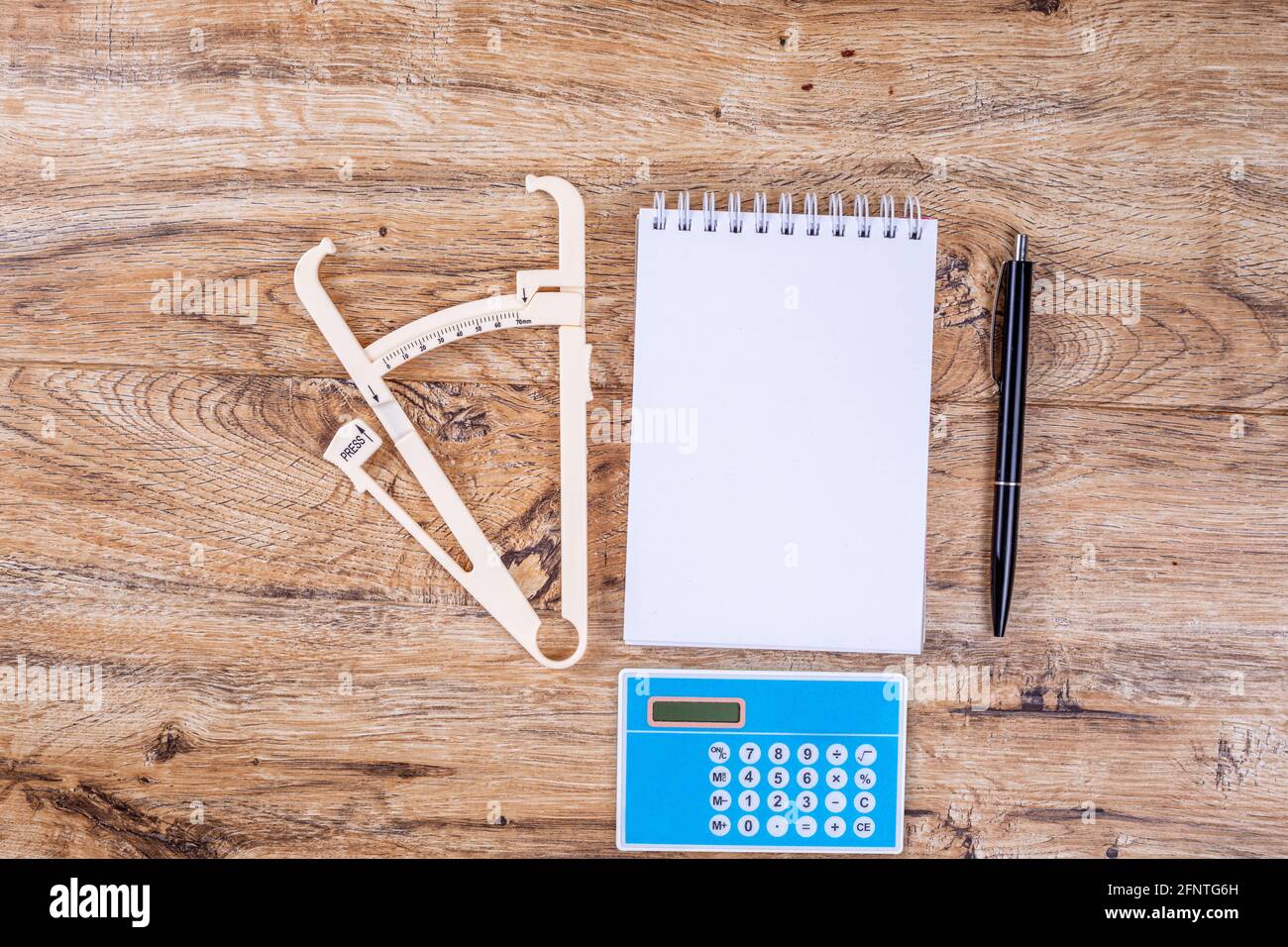 Blank sheet of notepad pen calculator and caliper on wooden table top ...