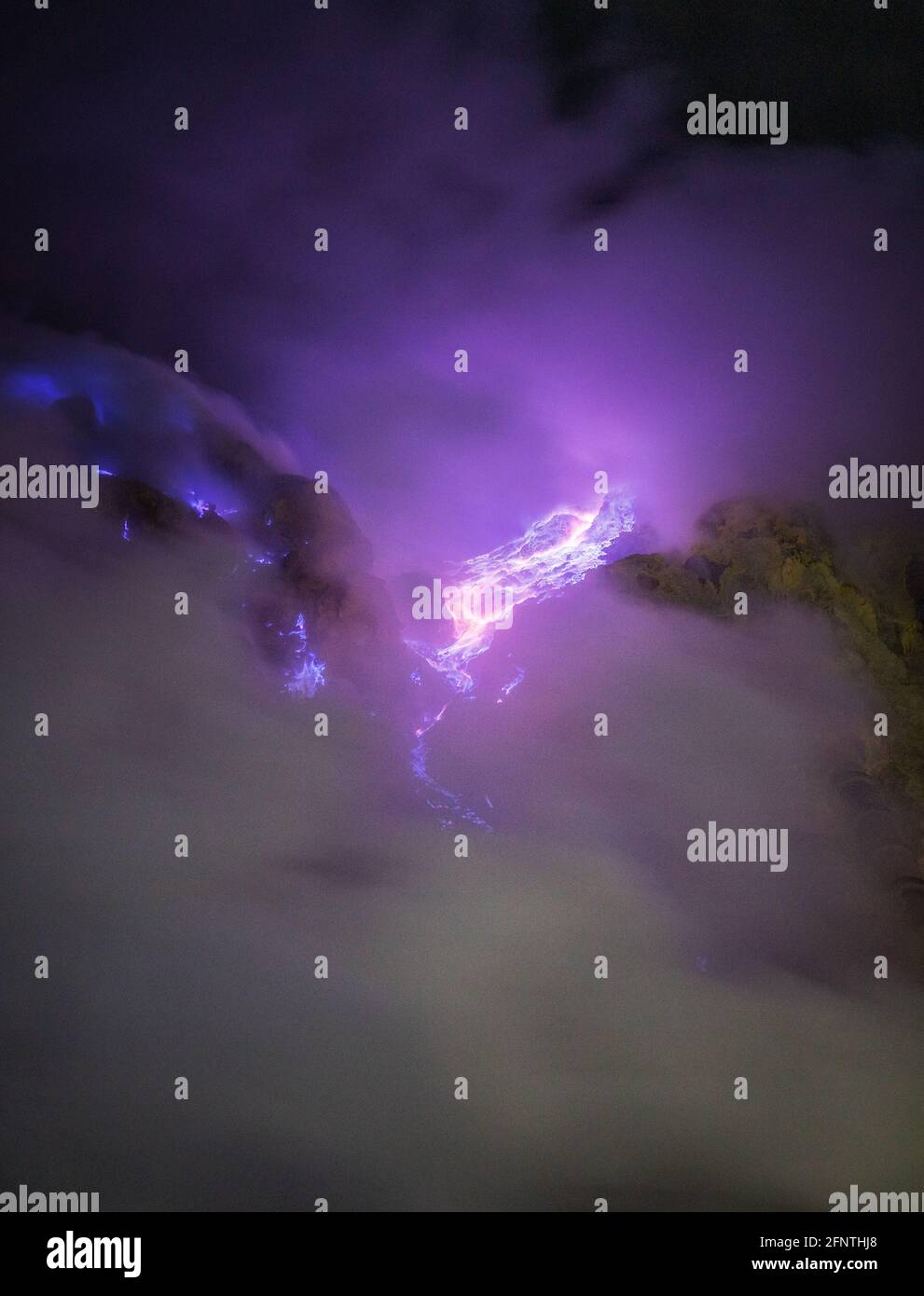 Vertical shot of a volcano with violet lava in the cloudy sky ...