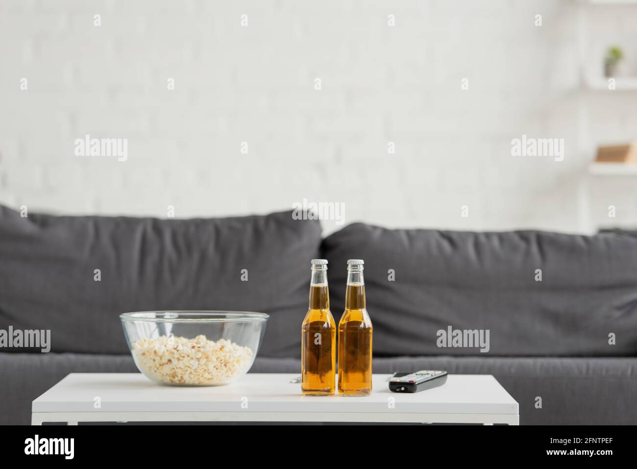 front view of two bottles of beer, popcorn and TV remote on blurred ...
