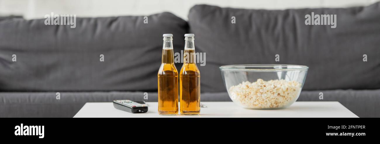 front view of two bottles of beer, popcorn and TV remote on blurred ...
