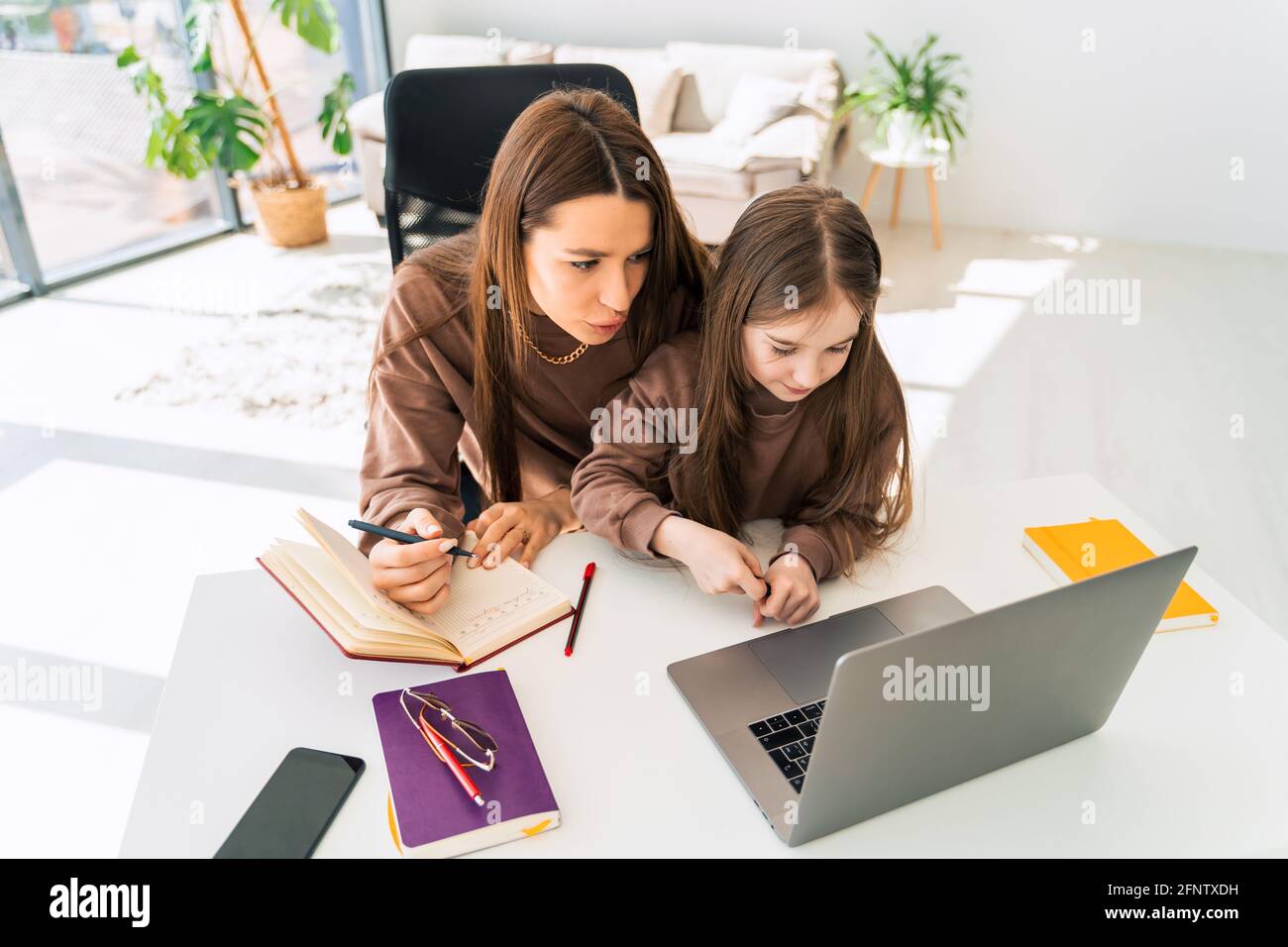 Mom and little daughter doing homework on laptop. Mother teaches the ...