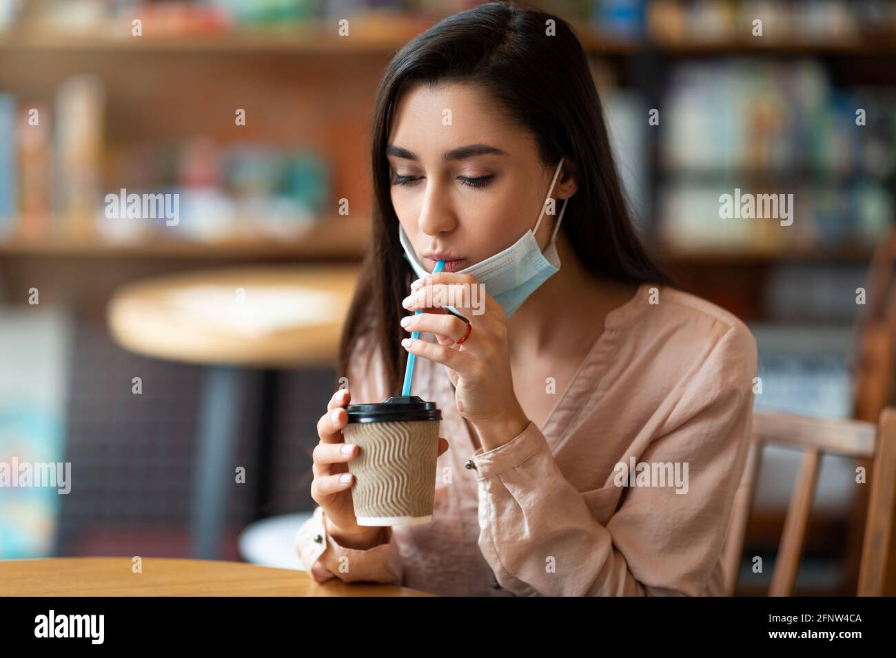 Arab lady drinking coffee with straw in cafe after quarantine, lowered ...