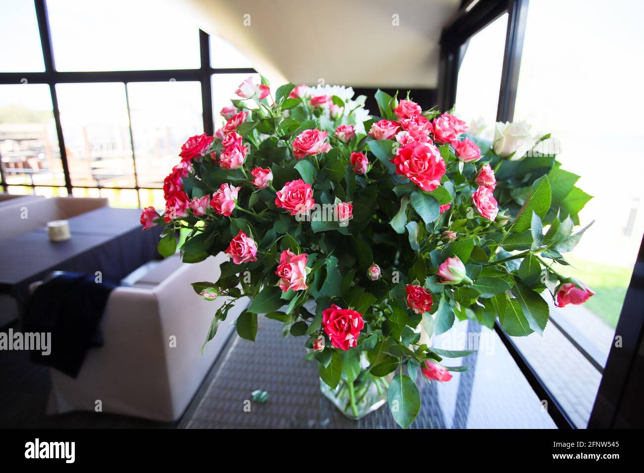 Small pink shrub roses in the vase opposite the window Stock Photo - Alamy