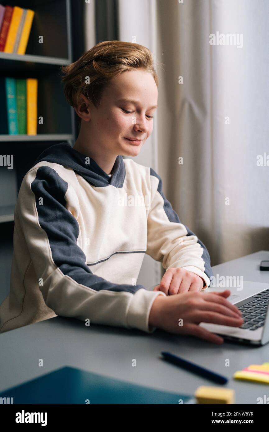 Close-up side view of smiling happy child boy using typing laptop ...