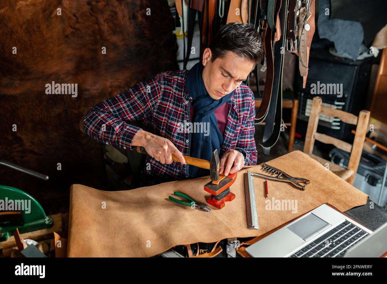 Young artisan man working with leather holding a hammer. Work tools in ...