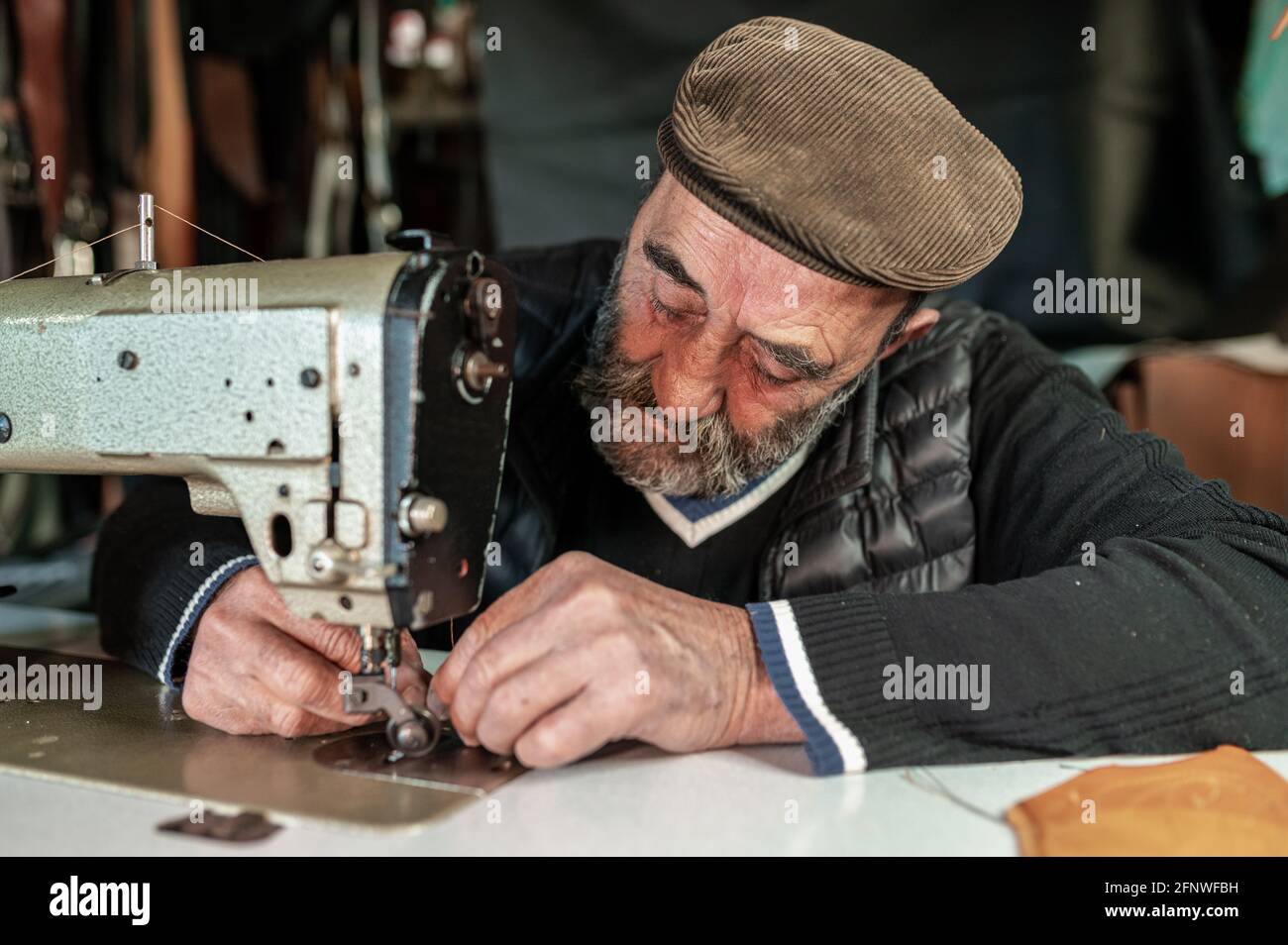 Old hipster bearded man with flat cap setting a sewing machine ...