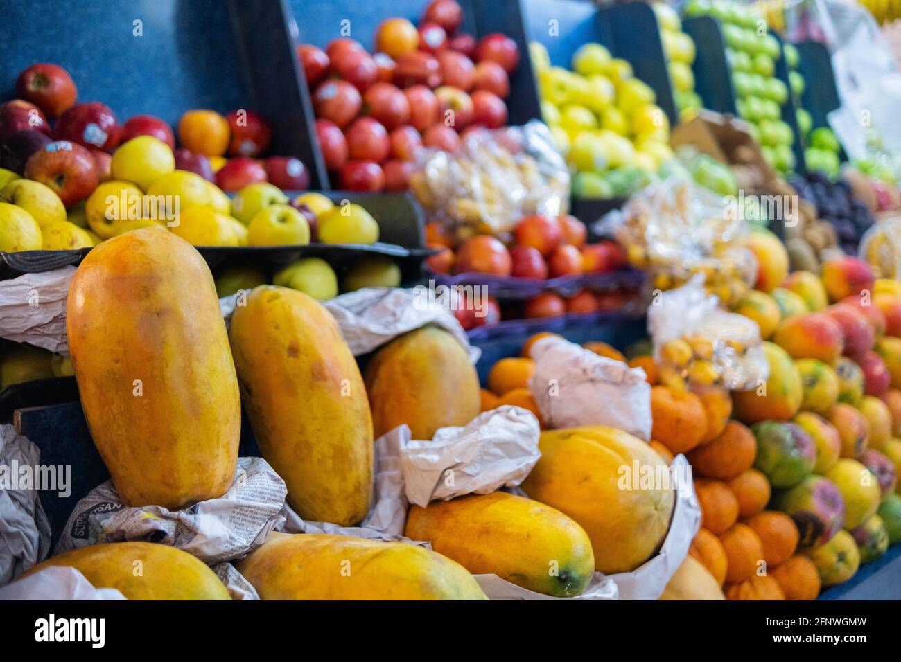 Colorful fruit stand with papayas, red and yellow apples, and more ...
