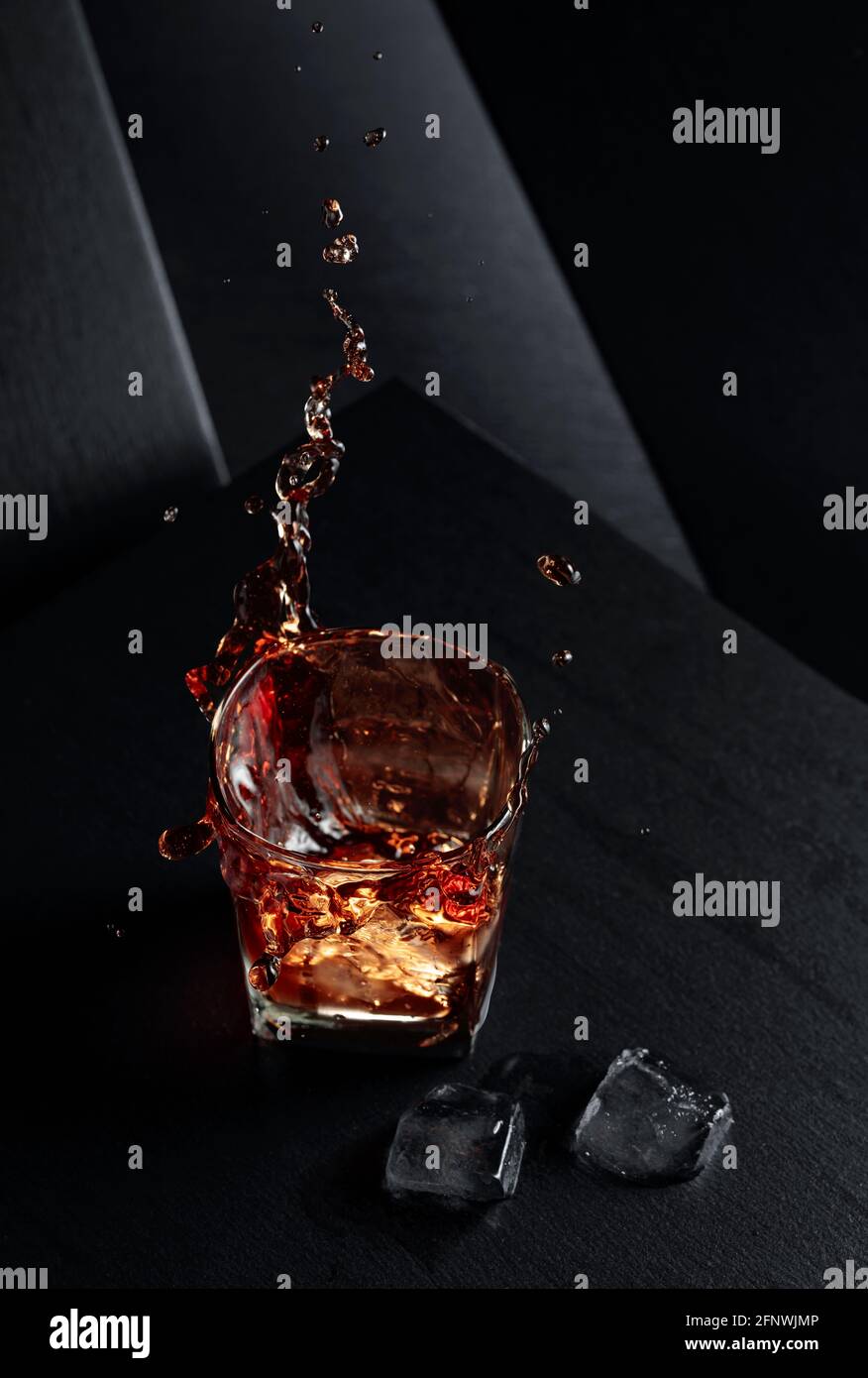 Ice cubes fall into a glass of whiskey creating splashes Stock Photo - Alamy