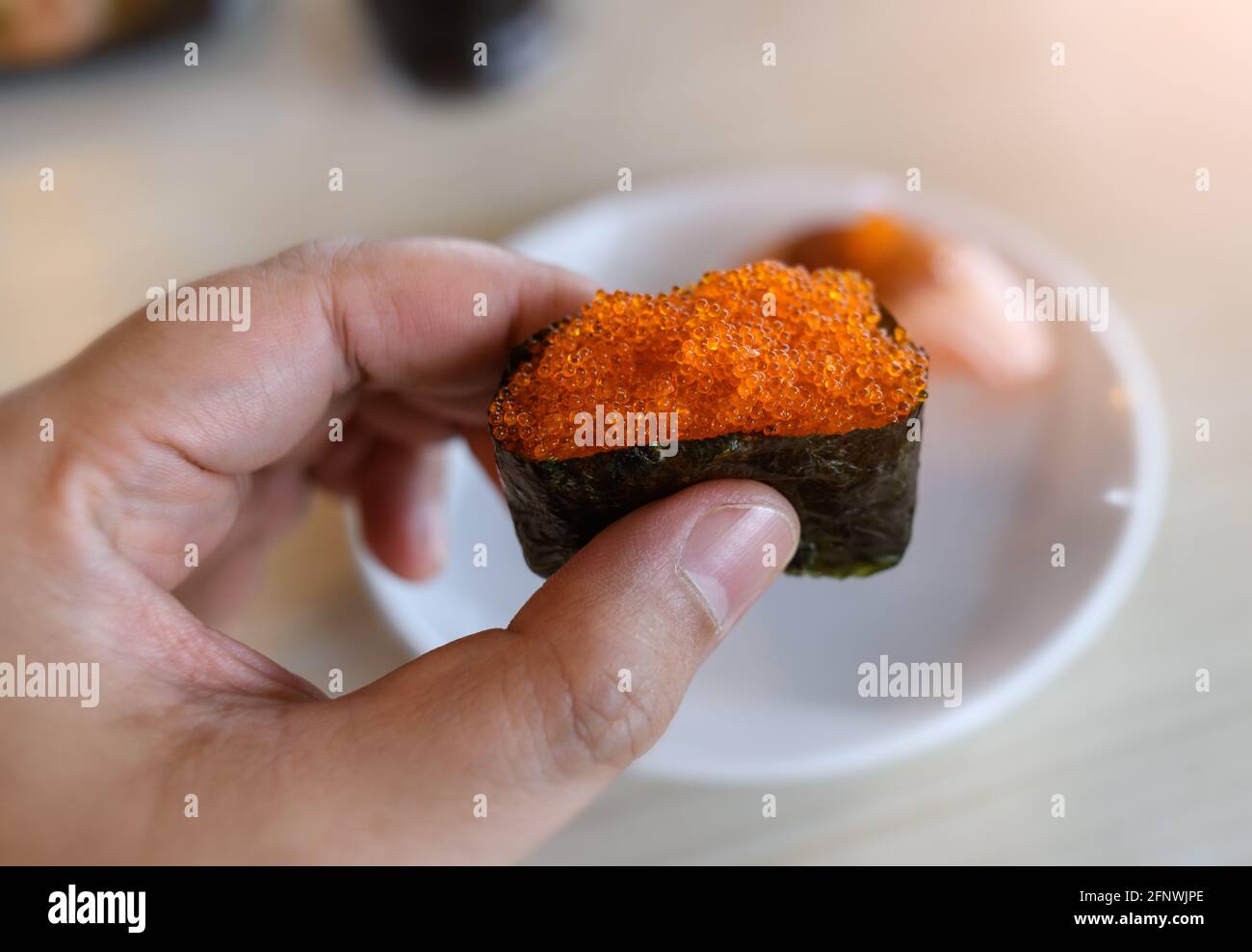 Gunkan sushi from tobiko flying fish roe in hand with indoor low ...