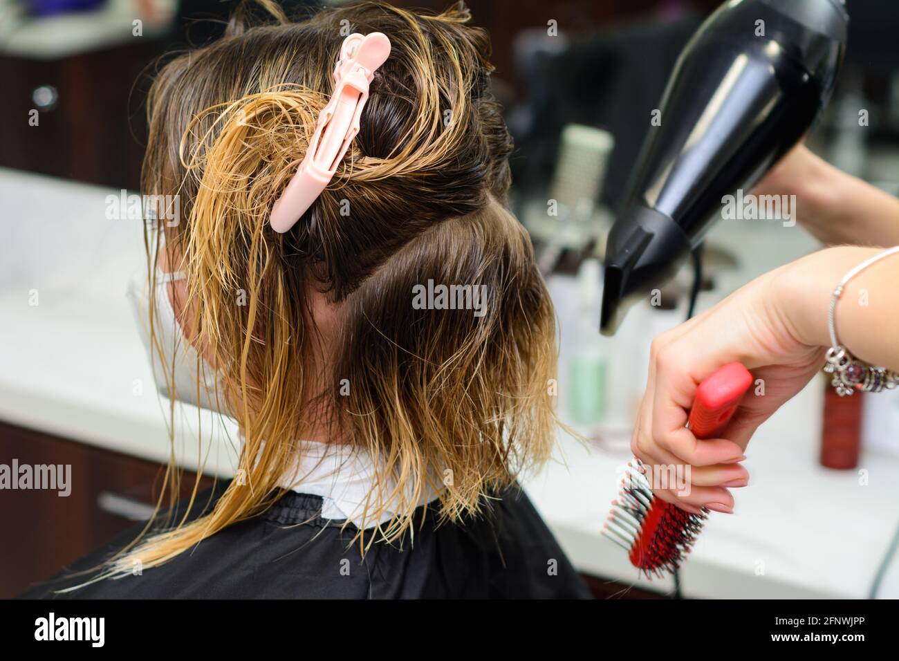 Hairdresser in a mask with at work, drying hair in a barbershop, client ...