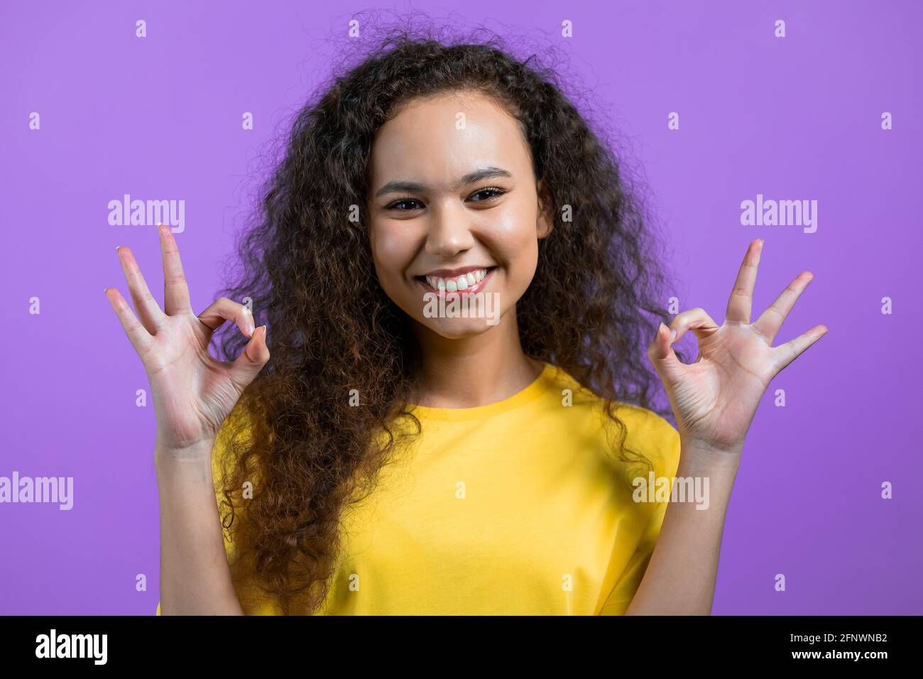 Pretty woman showing ok, okay sign over purple studio background ...