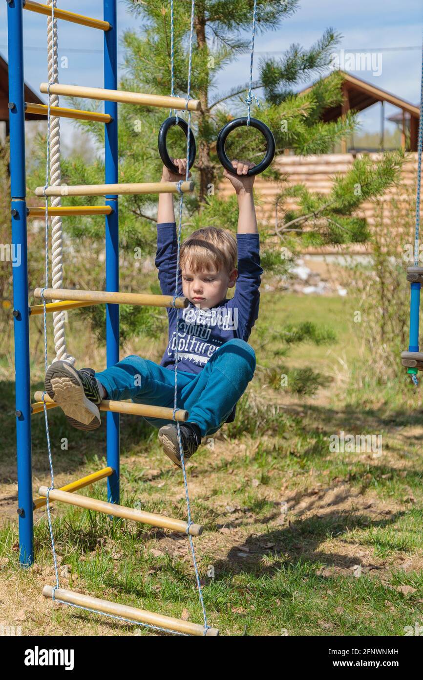 A blonde-haired child is playing on the playground, hanging on rings ...