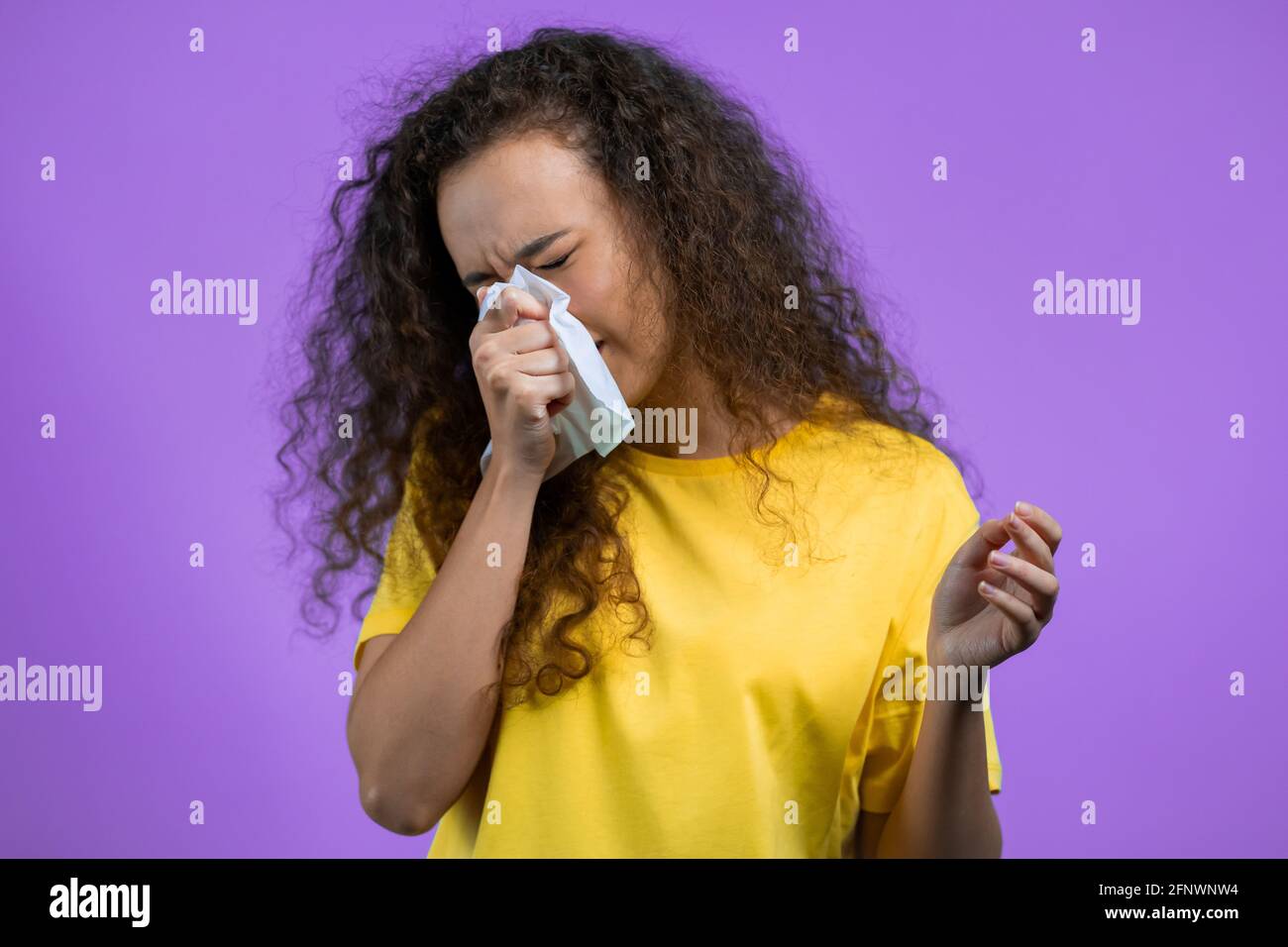 Pretty woman sneezes into tissue. Isolated girl on purple studio ...