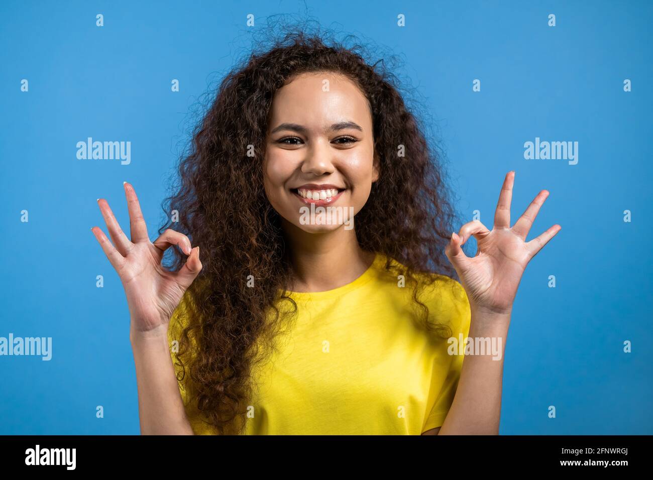 Pretty woman showing ok, okay sign over blue studio background ...