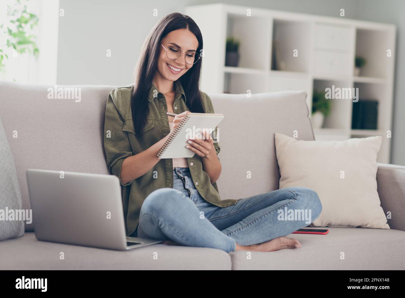 Portrait of lovely cheery girl sitting on divan lotus pose using laptop ...