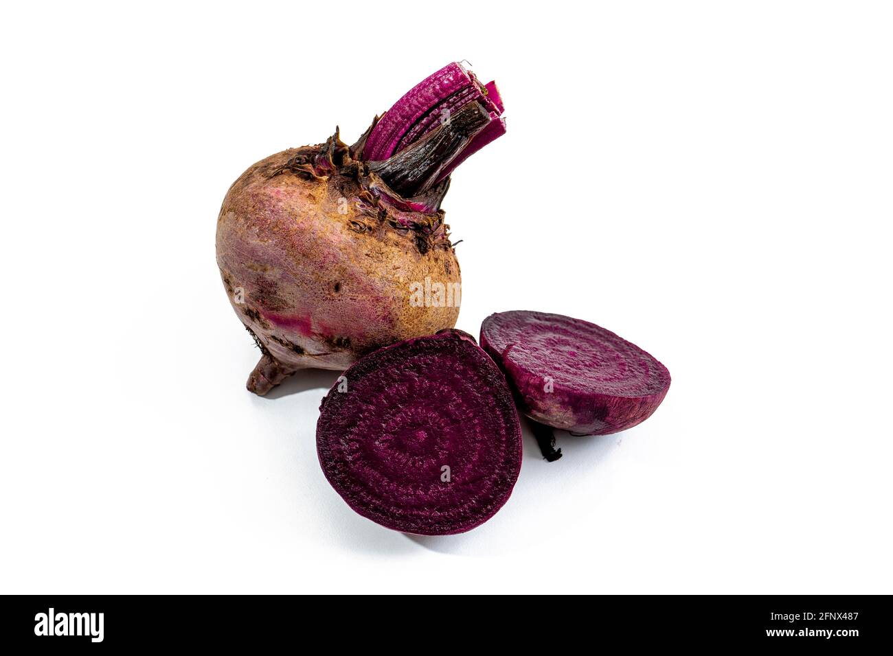 Whole leafless raw red beet root and a beet cut in half on a white ...