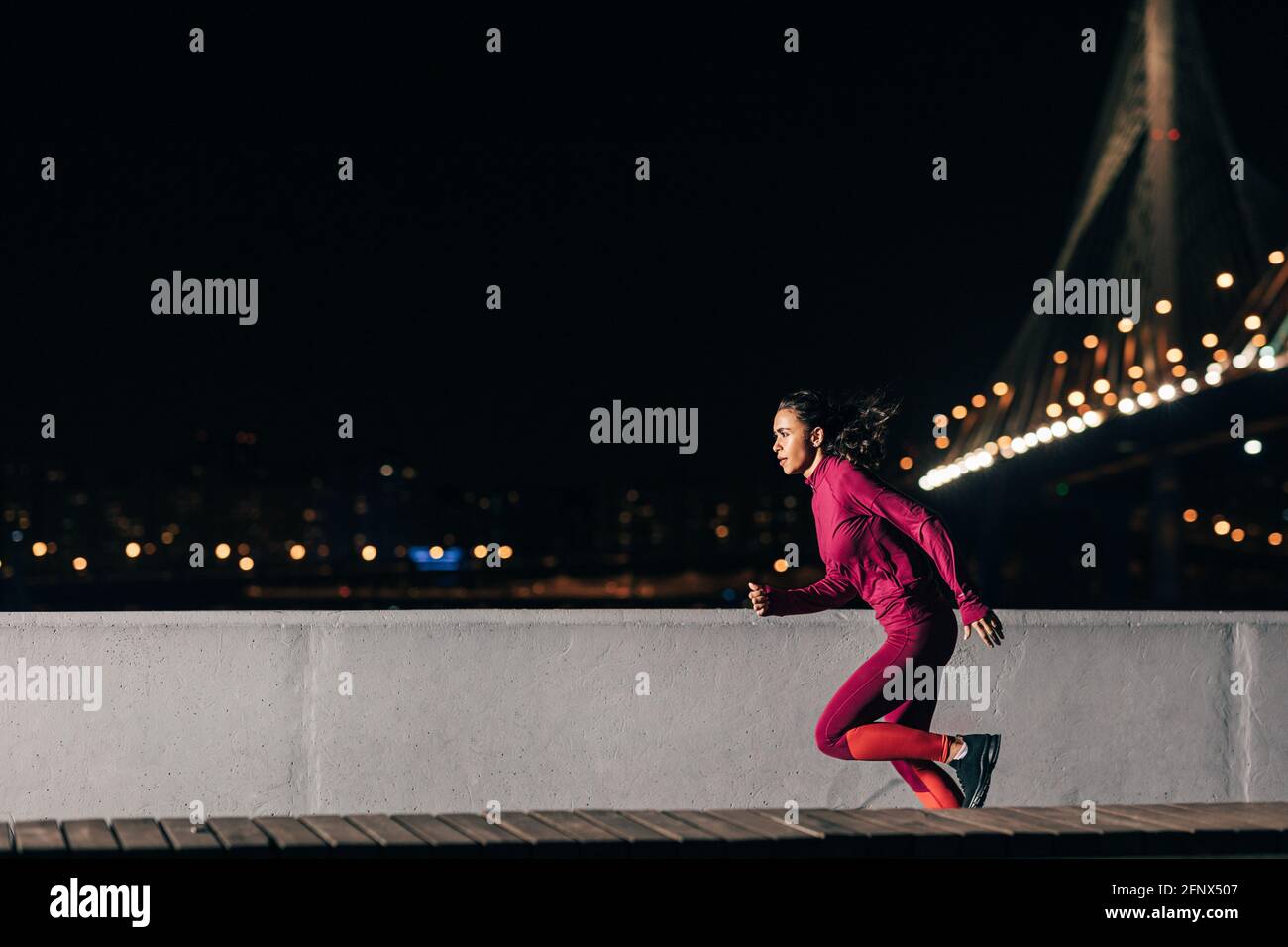Woman runner at night. Sportswoman sprinting outdoors against a bridge ...