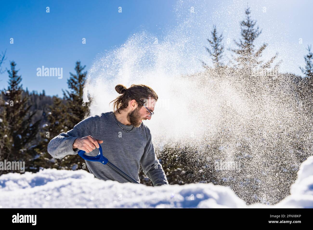 Side view of a young man energetically throwing a heap of fresh snow ...