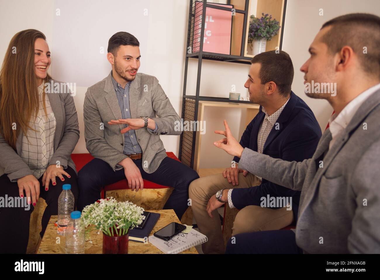Four young entrepreneurs talking in a pelsant office spot while smiling ...