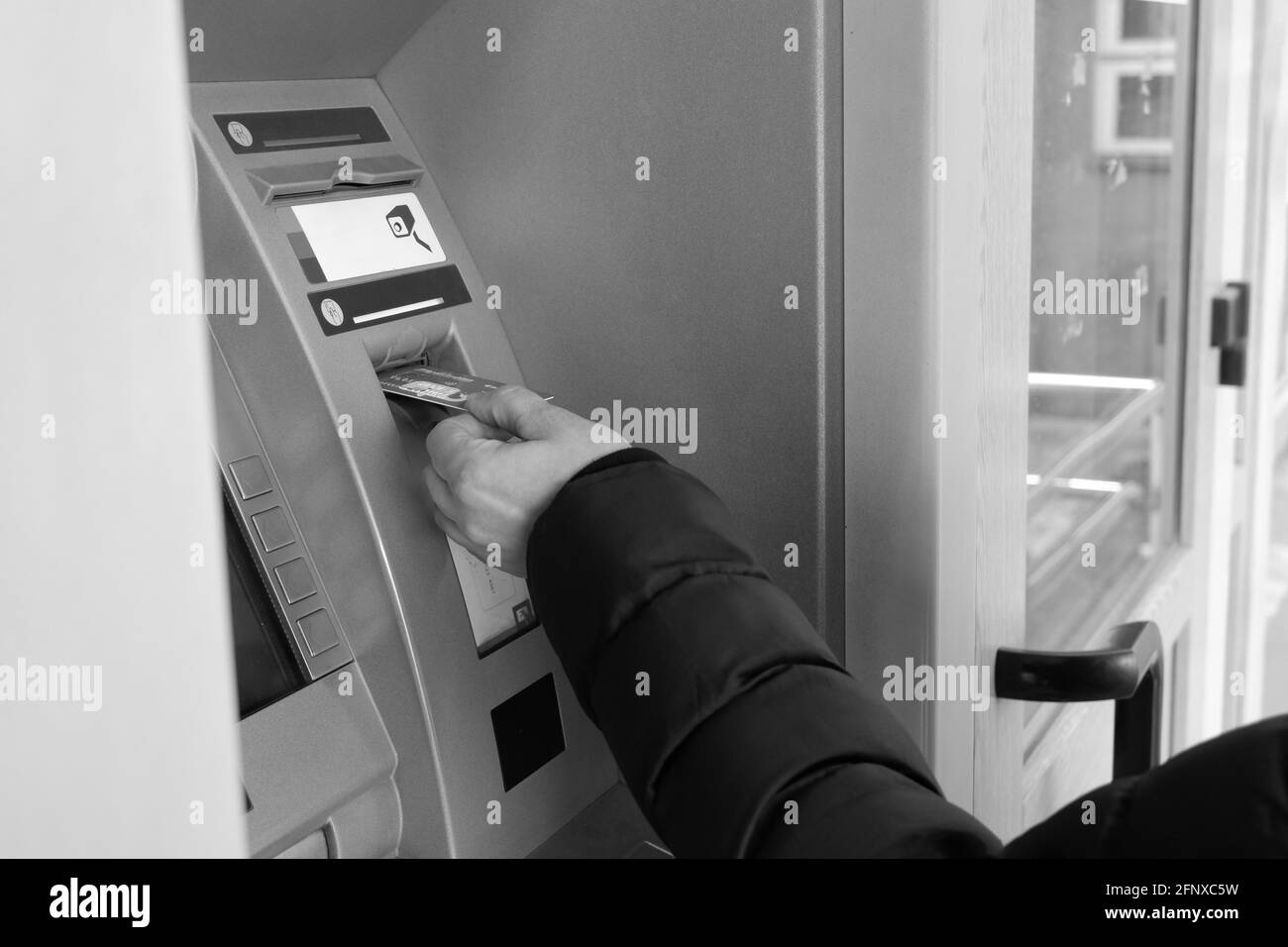 A man's hand inserts a credit card into an ATM machine. Black and white ...