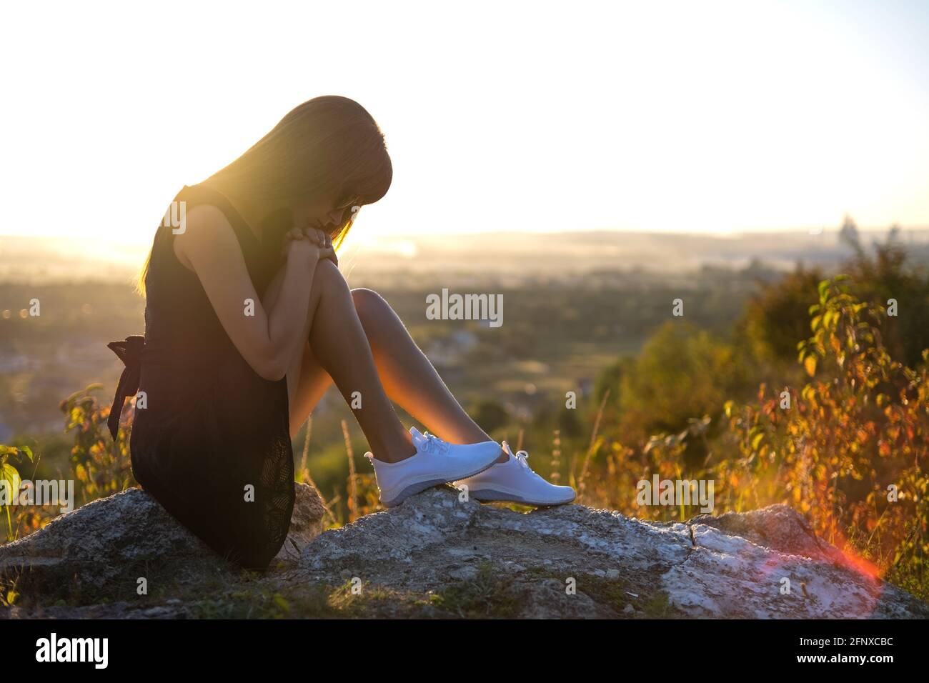 Young depressed woman in black short summer dress sitting on a rock ...