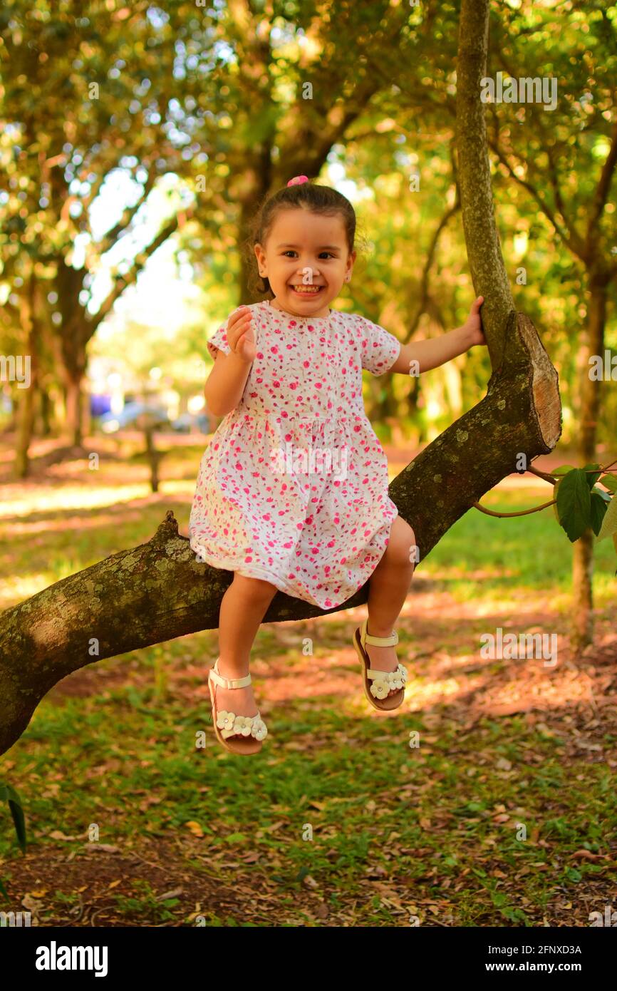 Vertical shot of a happy caucasian little girl sitting on a branch ...