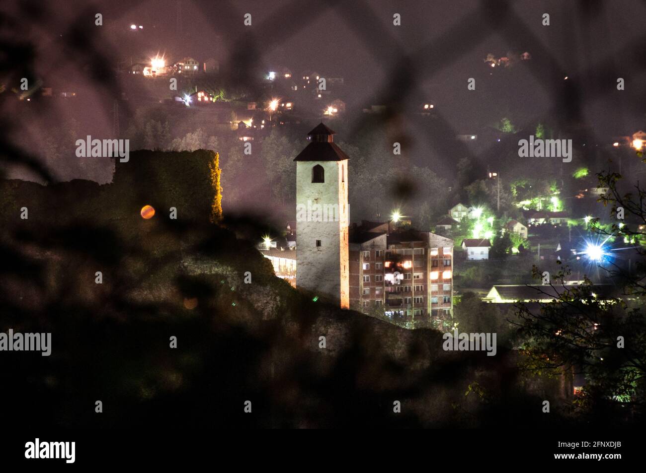 Night cityscape with a medieval watchtower seen behind the metallic ...