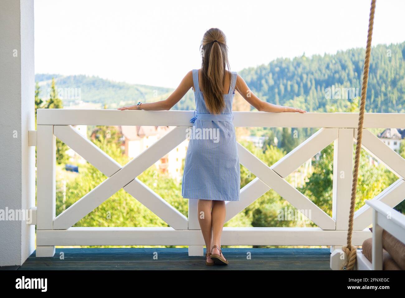 Back view of young beautiful woman at balcony enjoying nature view ...