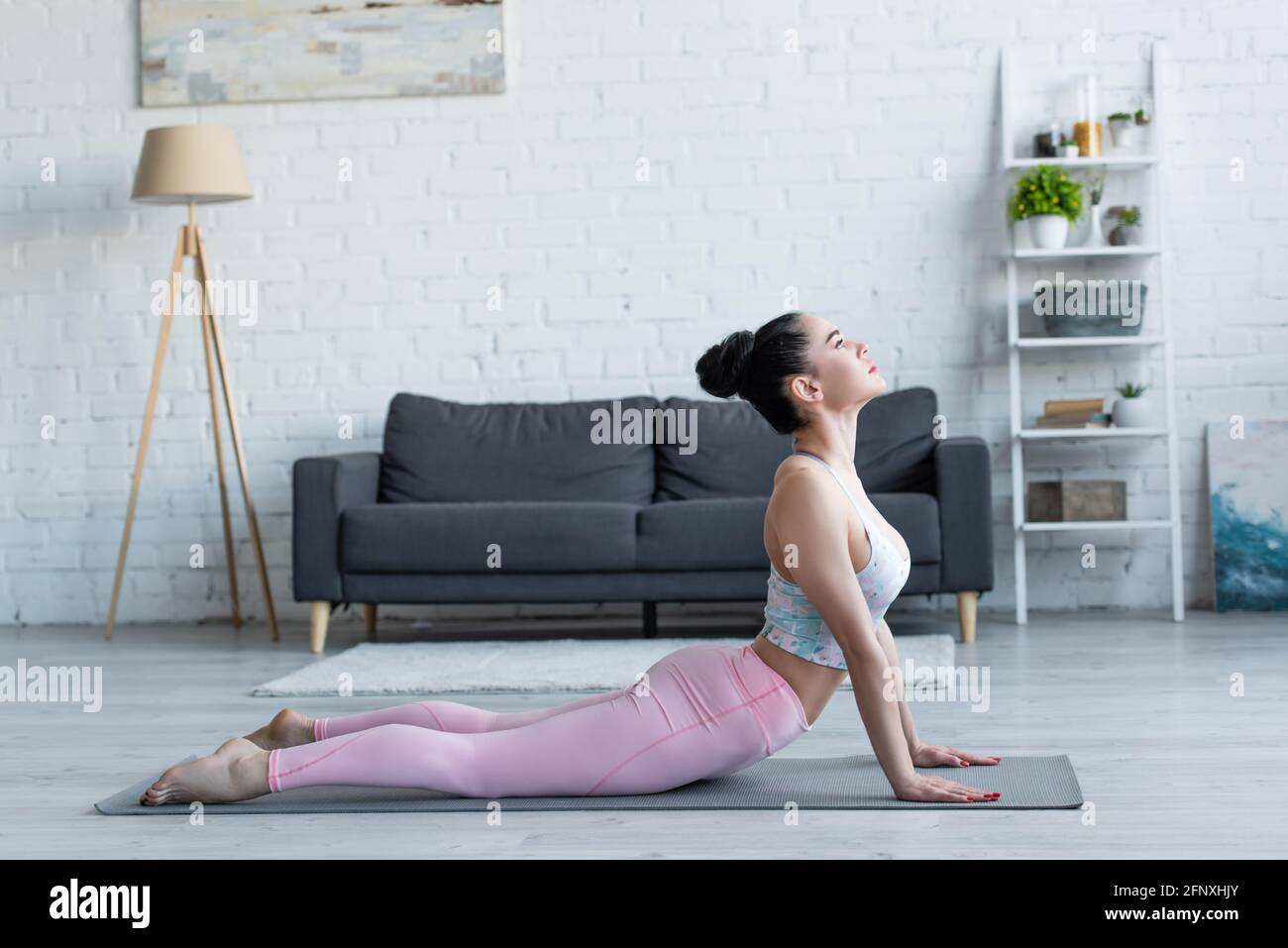 side view of young brunette woman practicing yoga in high cobra pose ...