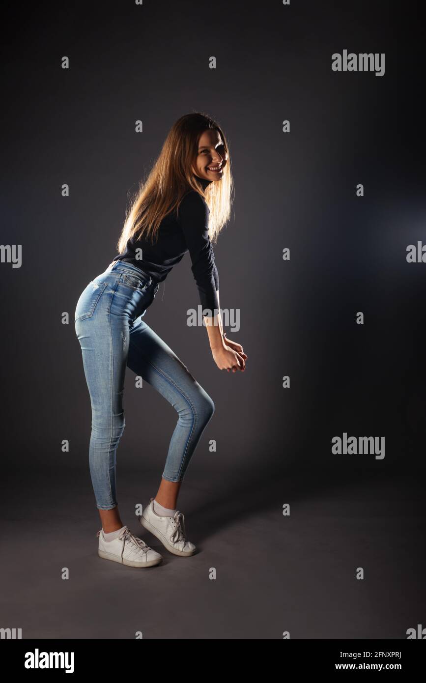 Side full-body portrait of a young female model in black top and jeans ...