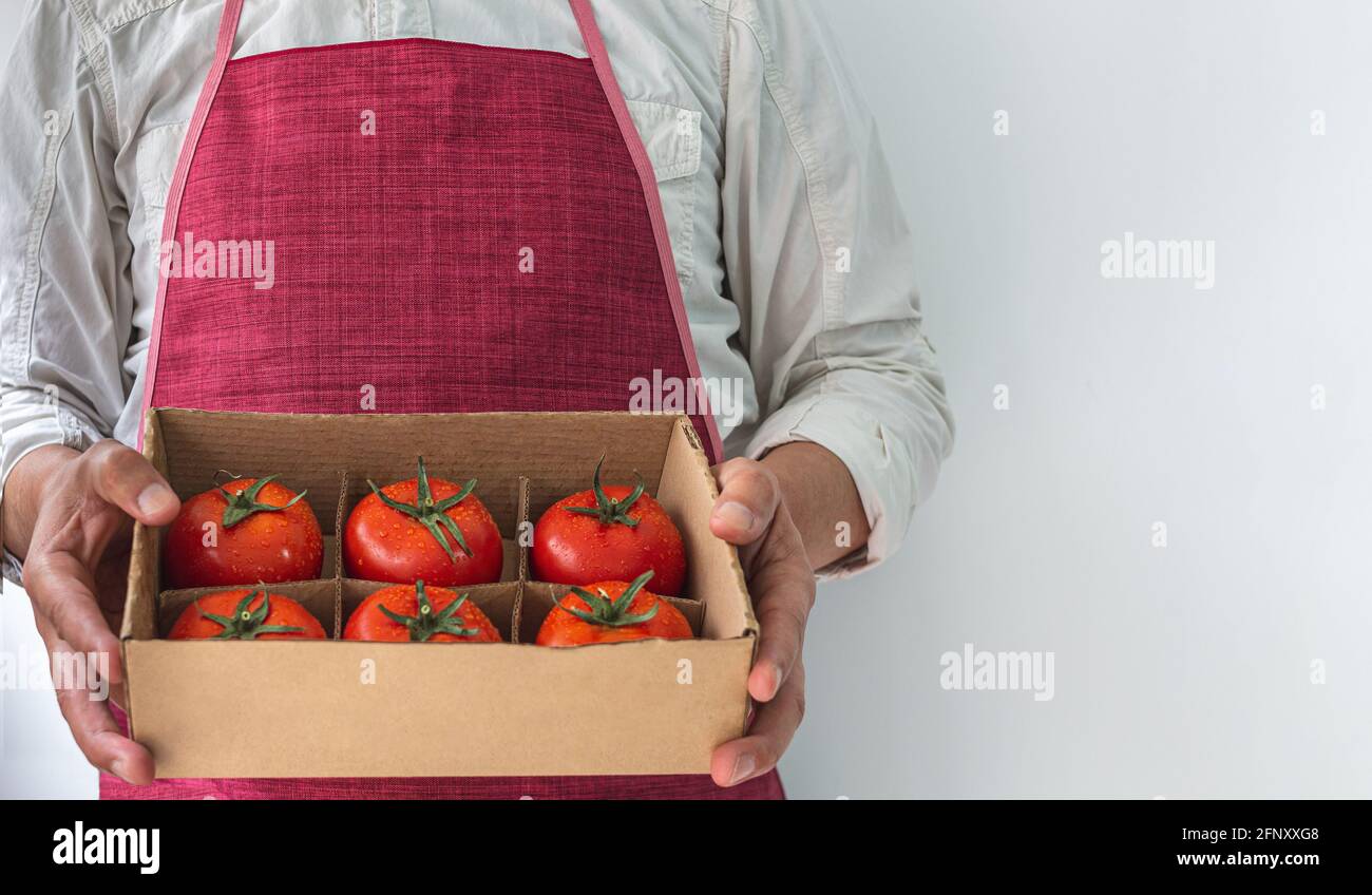Front shot of an unrecognizable farmer in red apron carrying a box of ...