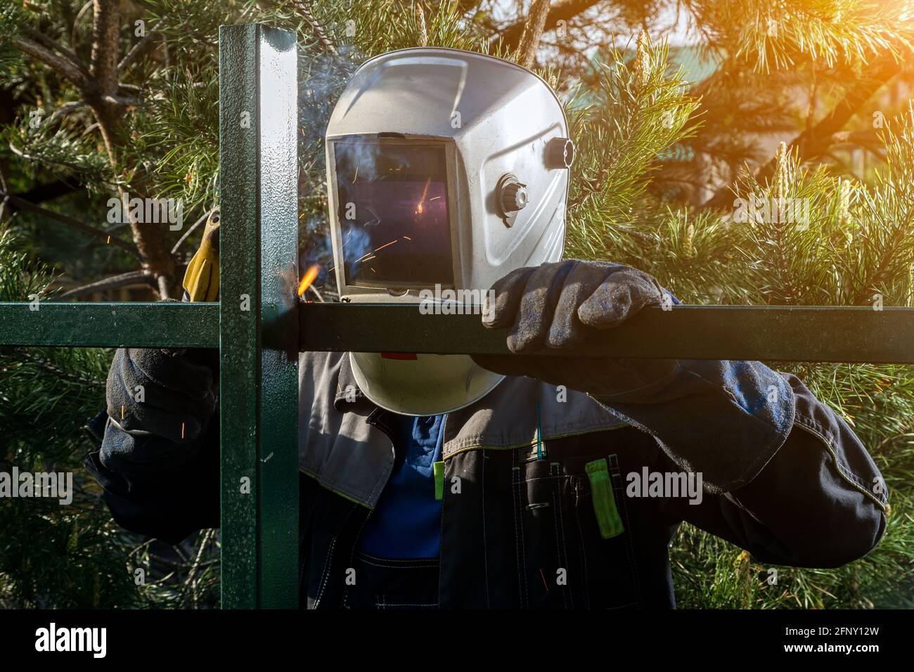 The welder welds a new metal frame for the fence around the house in ...
