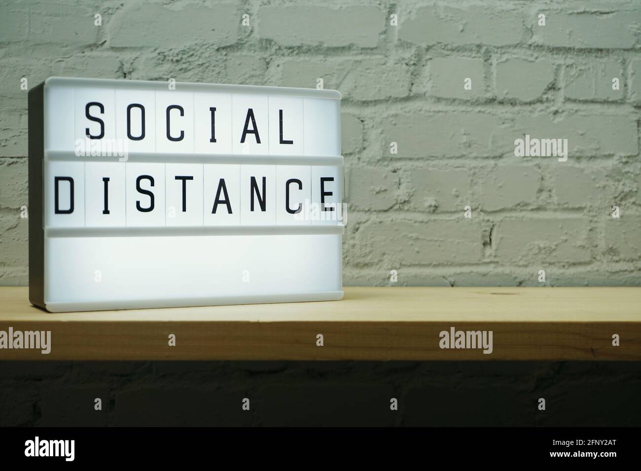 Social Distance word in light box on wooden shelve and white brick wall ...